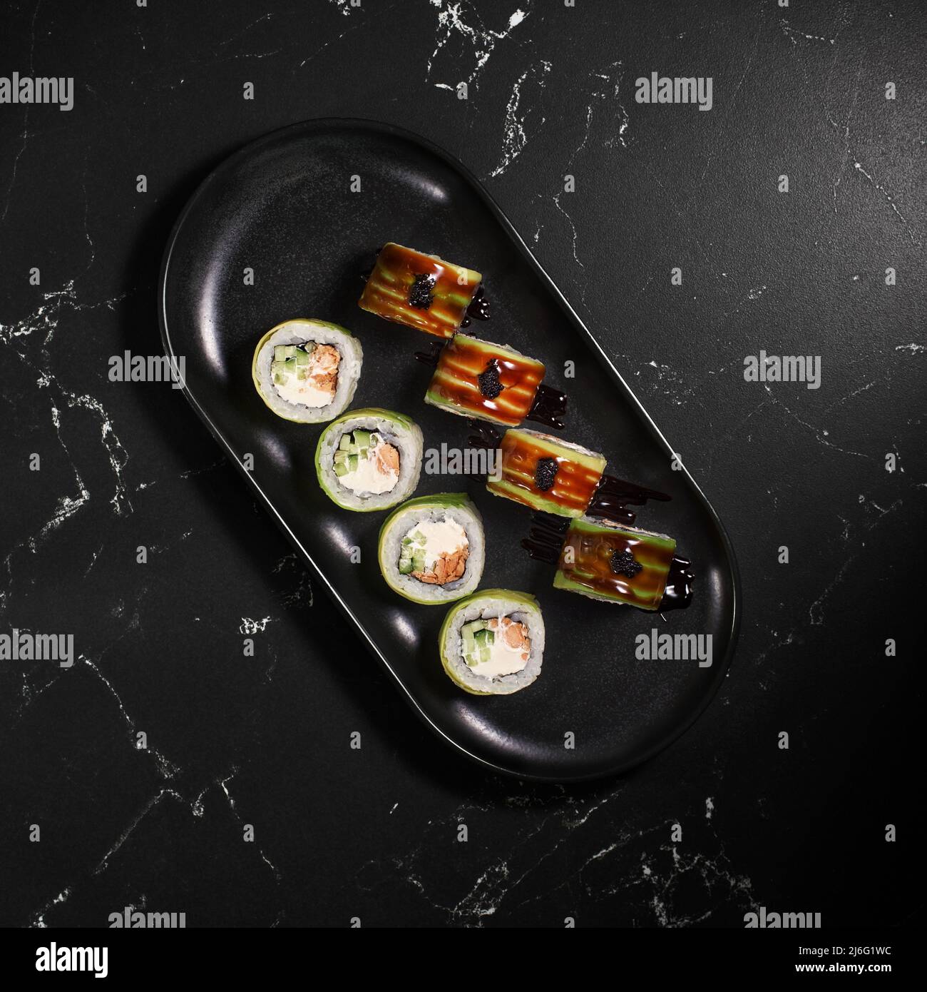 Green Dragon. uramaki sushi roll with smoked eel unagi covered by avocado on a black textured ...