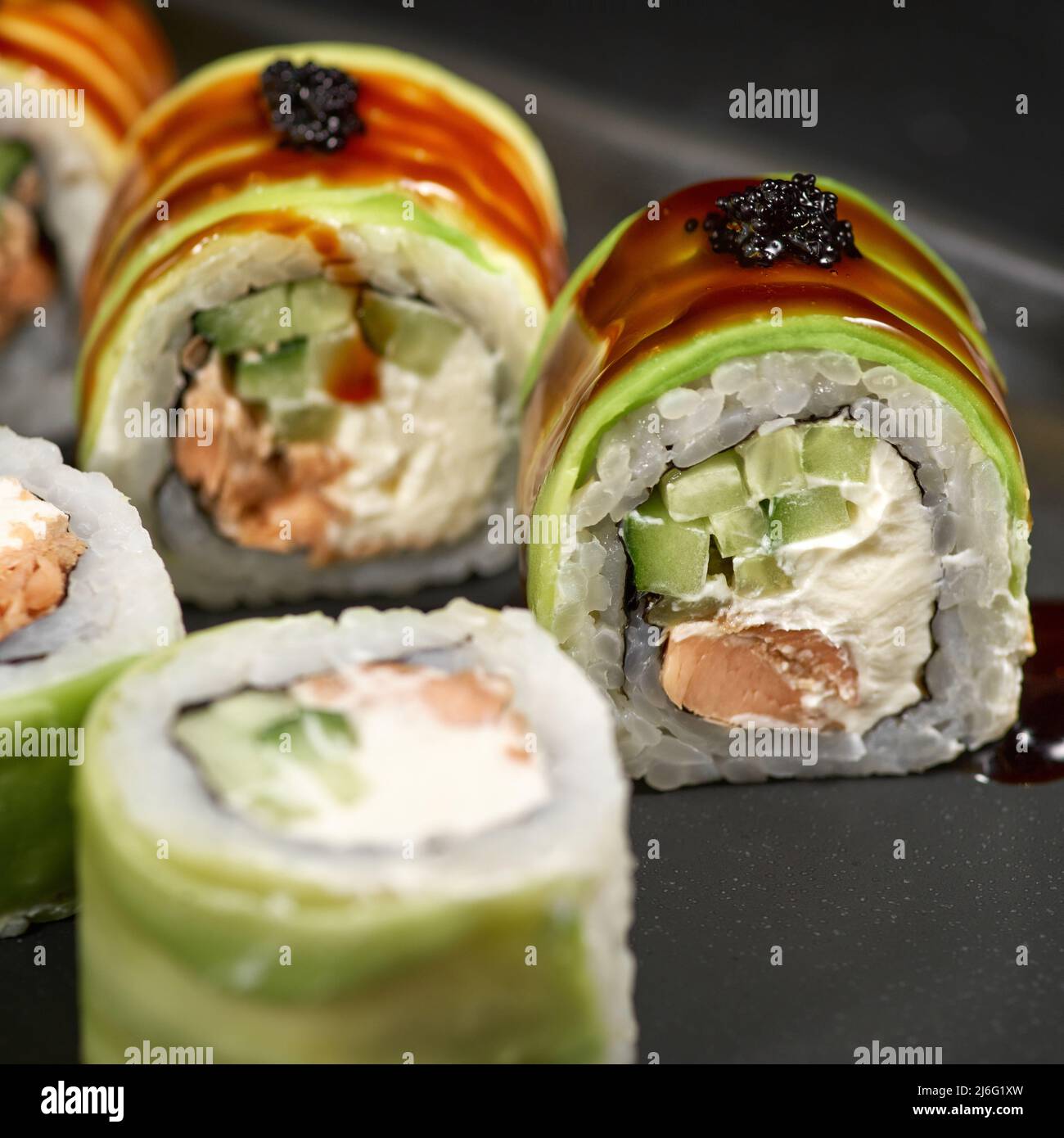 uramaki sushi roll with smoked eel unagi covered by avocado on a black textured background ...