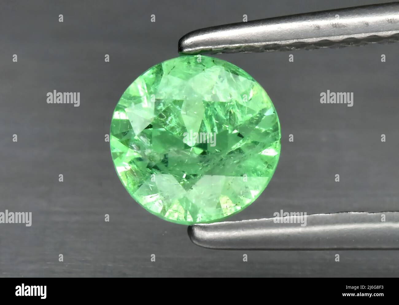 Natural gemstone green garnet tsavorite in tweezers on a background ...