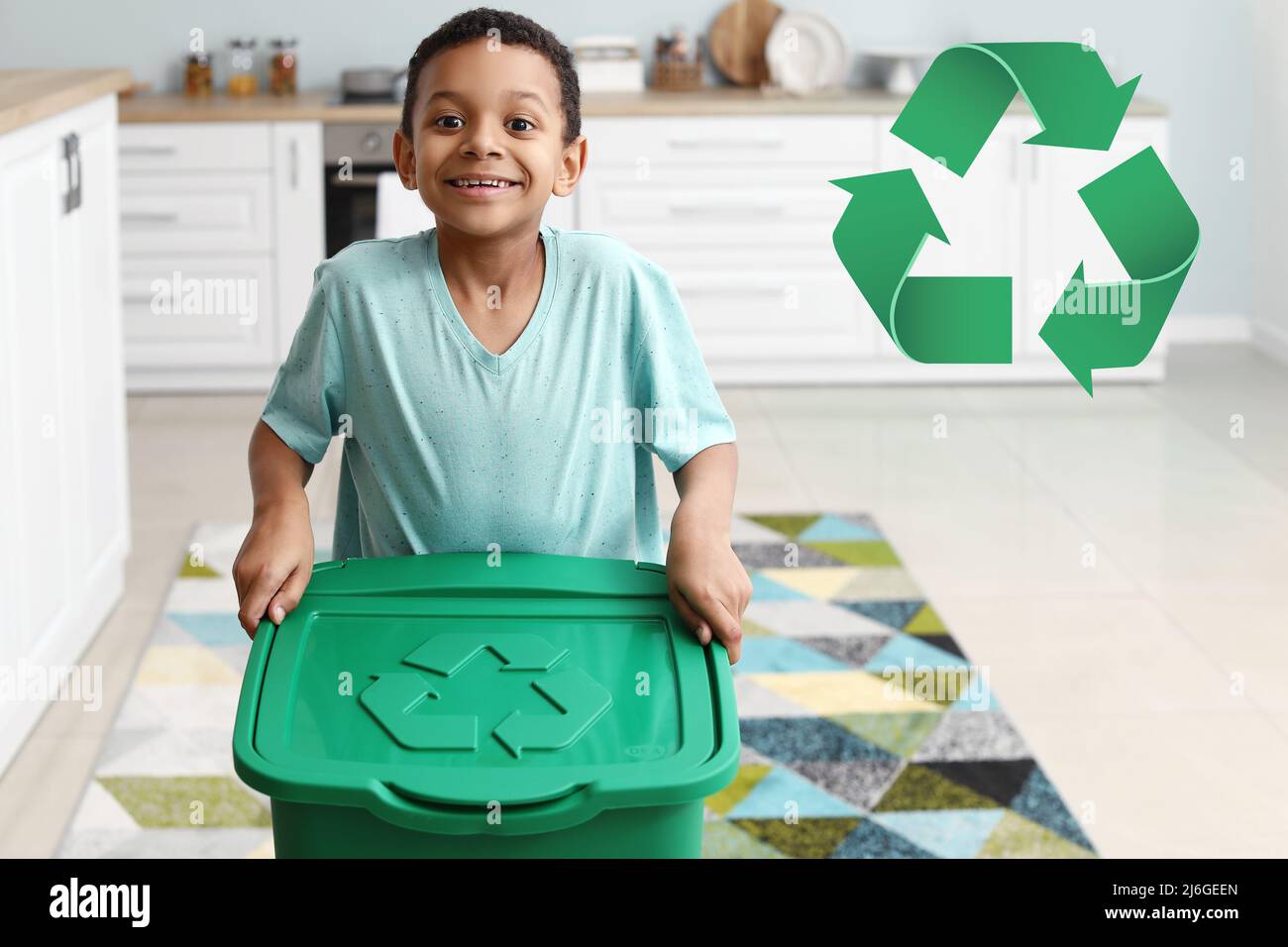 Little African-American boy and container with trash in kitchen ...