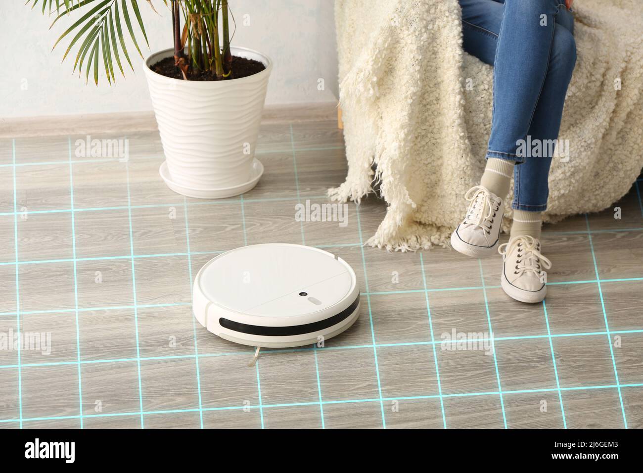 Modern robot vacuum cleaner on floor near woman sitting in armchair ...