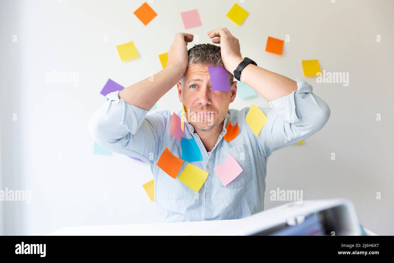 Man sits behind white office desk in front of wall with many colorful ...