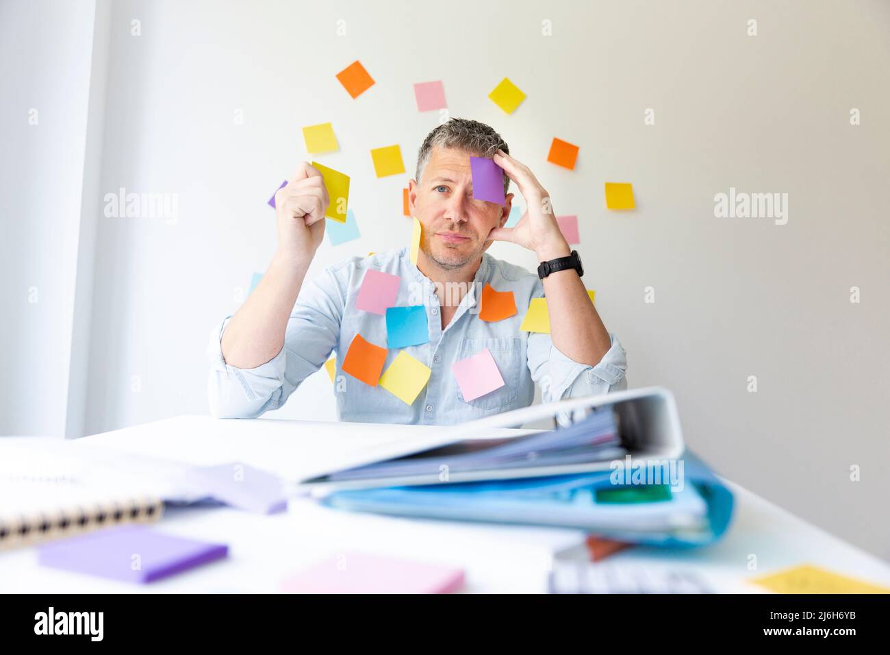 Man sits behind white office desk in front of wall with many colorful ...