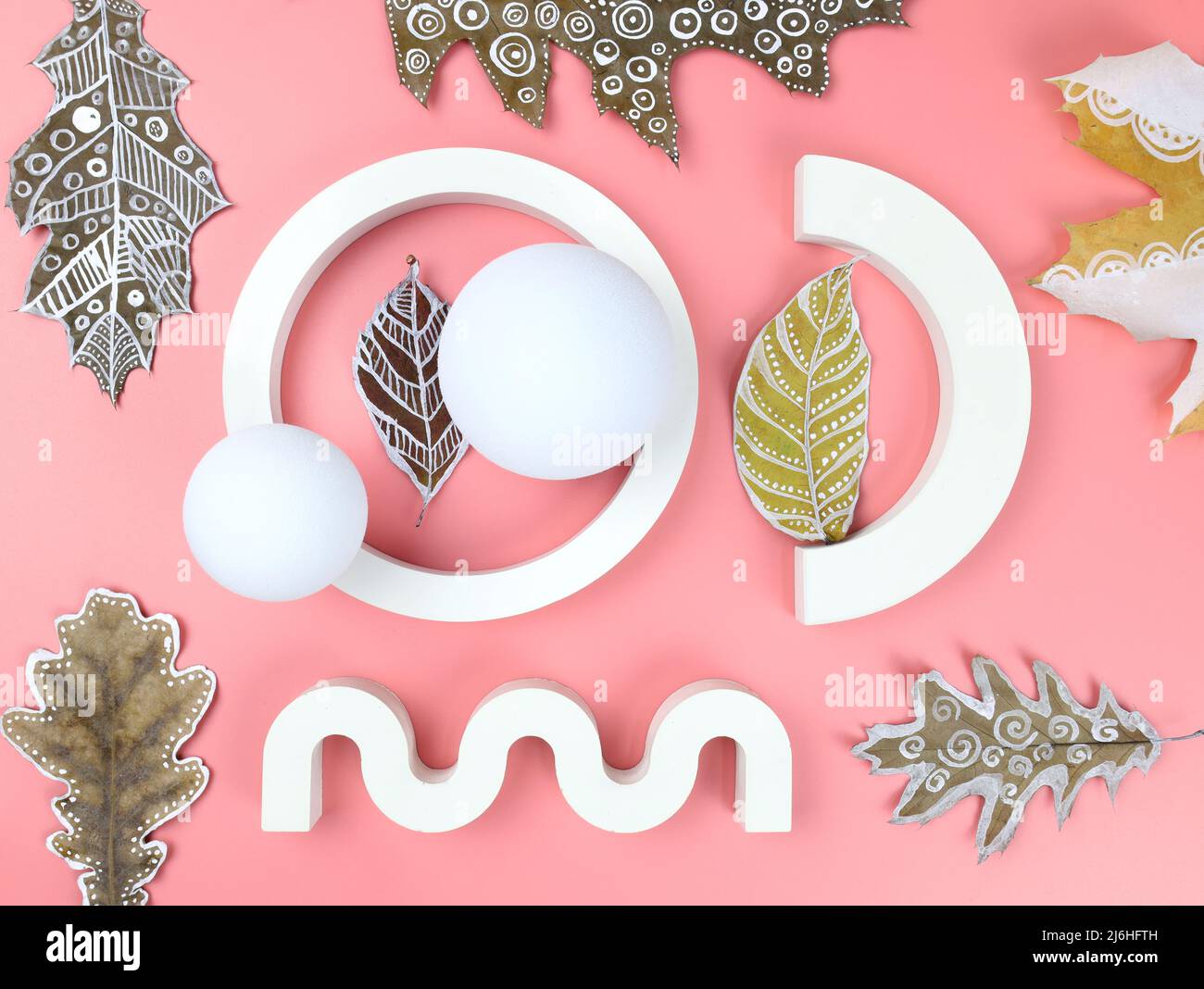 Gypsum figures of different shapes with dry autumn leaves on a pink ...