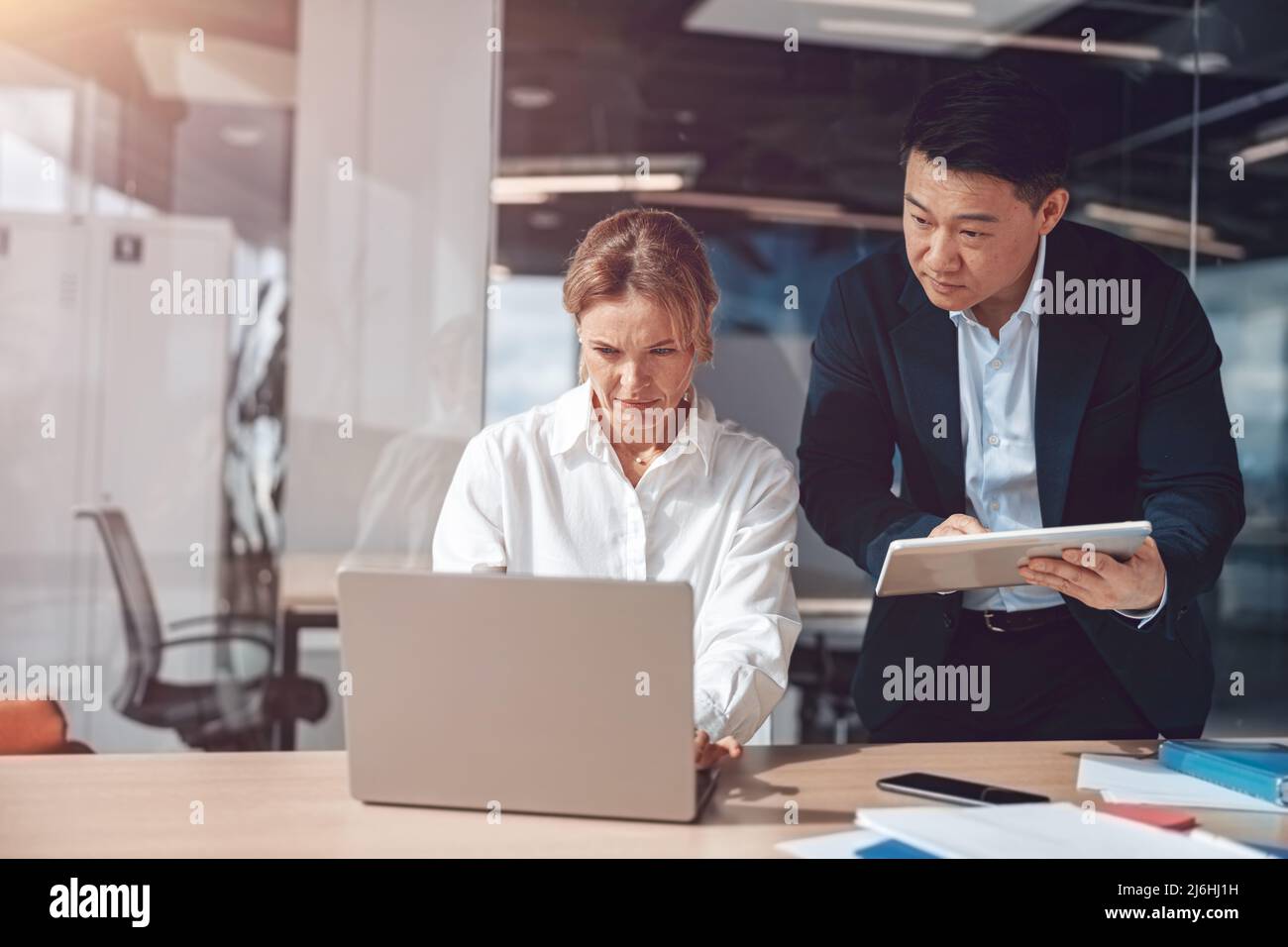Two diverse business people focused while working on a laptop together ...