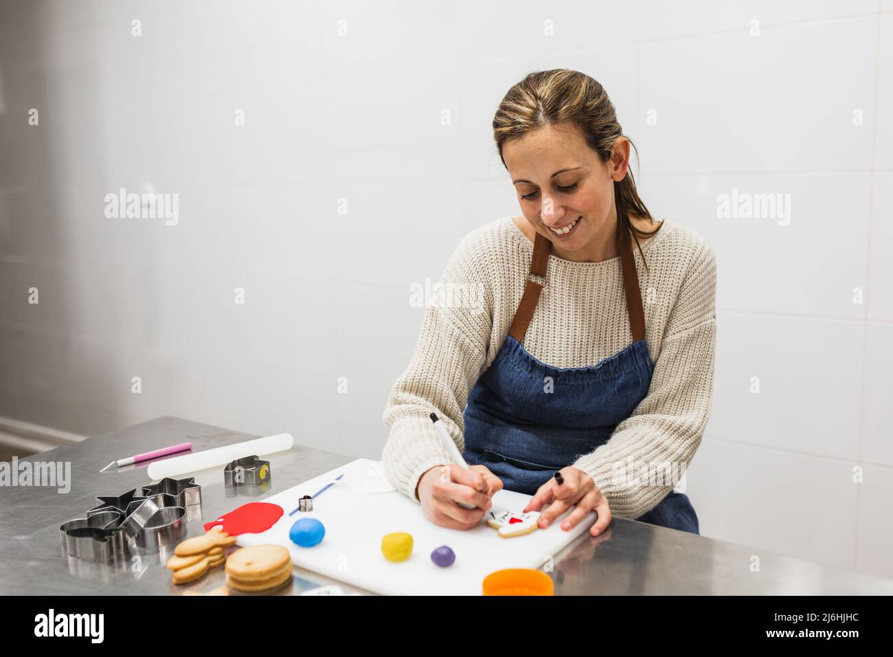 Positive and happy woman decorating cookies in bakery Stock Photo - Alamy