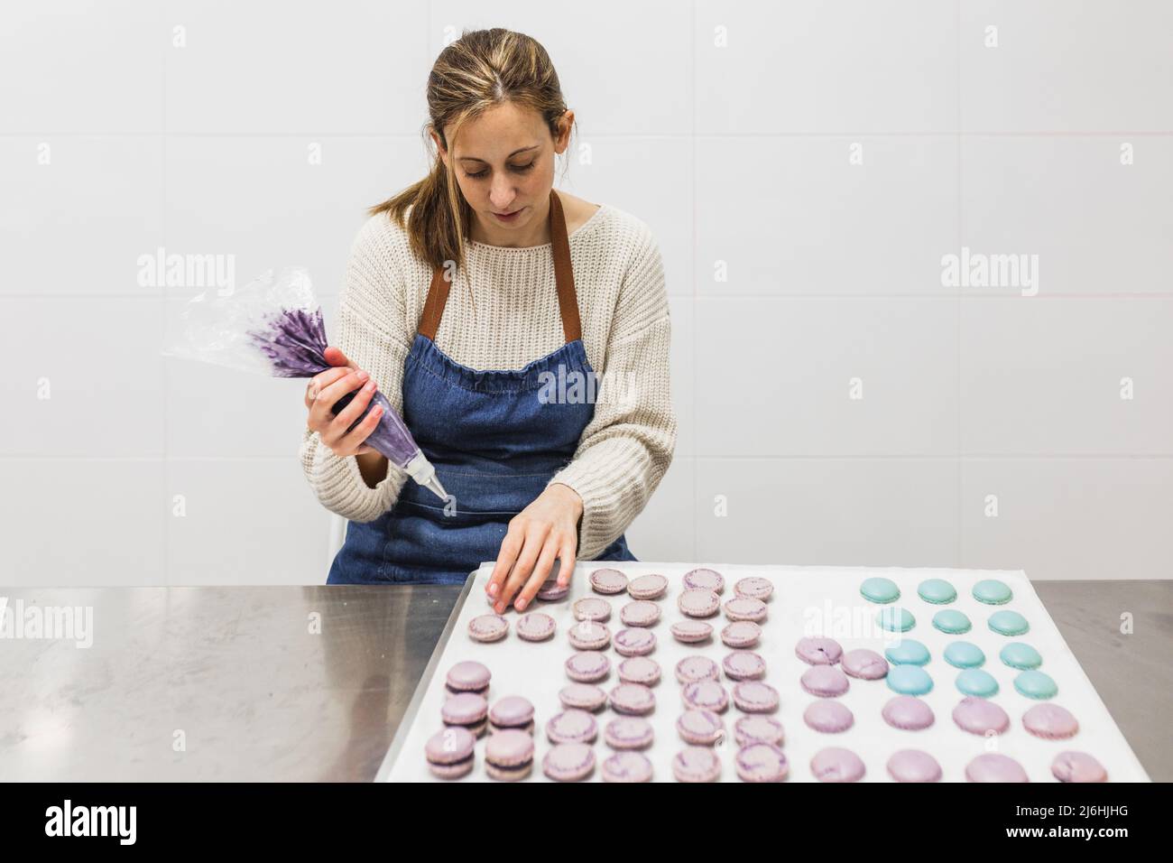 Pastry chef filling many macarons that are on tray on steel table Stock ...