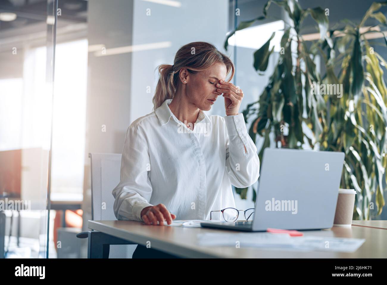 Tired lady boss with headache working on laptop at her workplace at ...