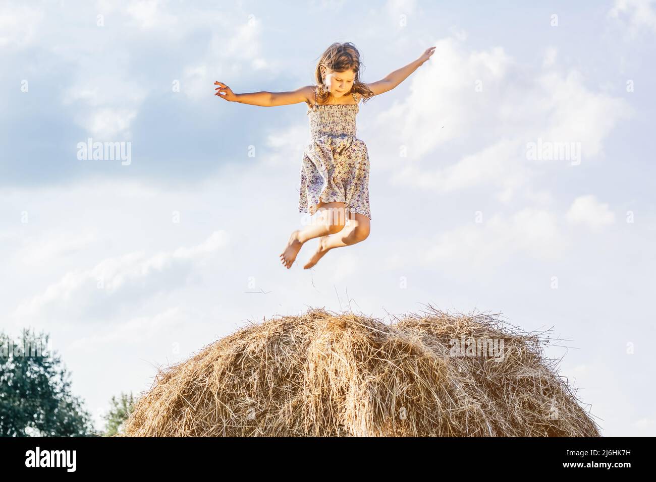 Portrait of little girl in dress playing and jumping on haystack in ...