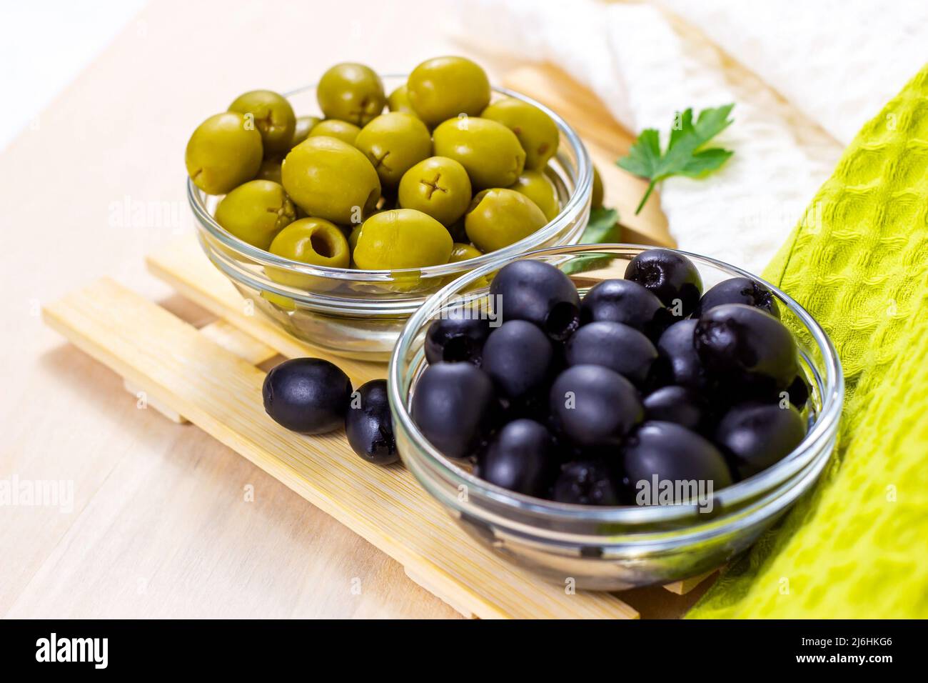 Many green and black marinated whole olives in the glass bowl on light ...