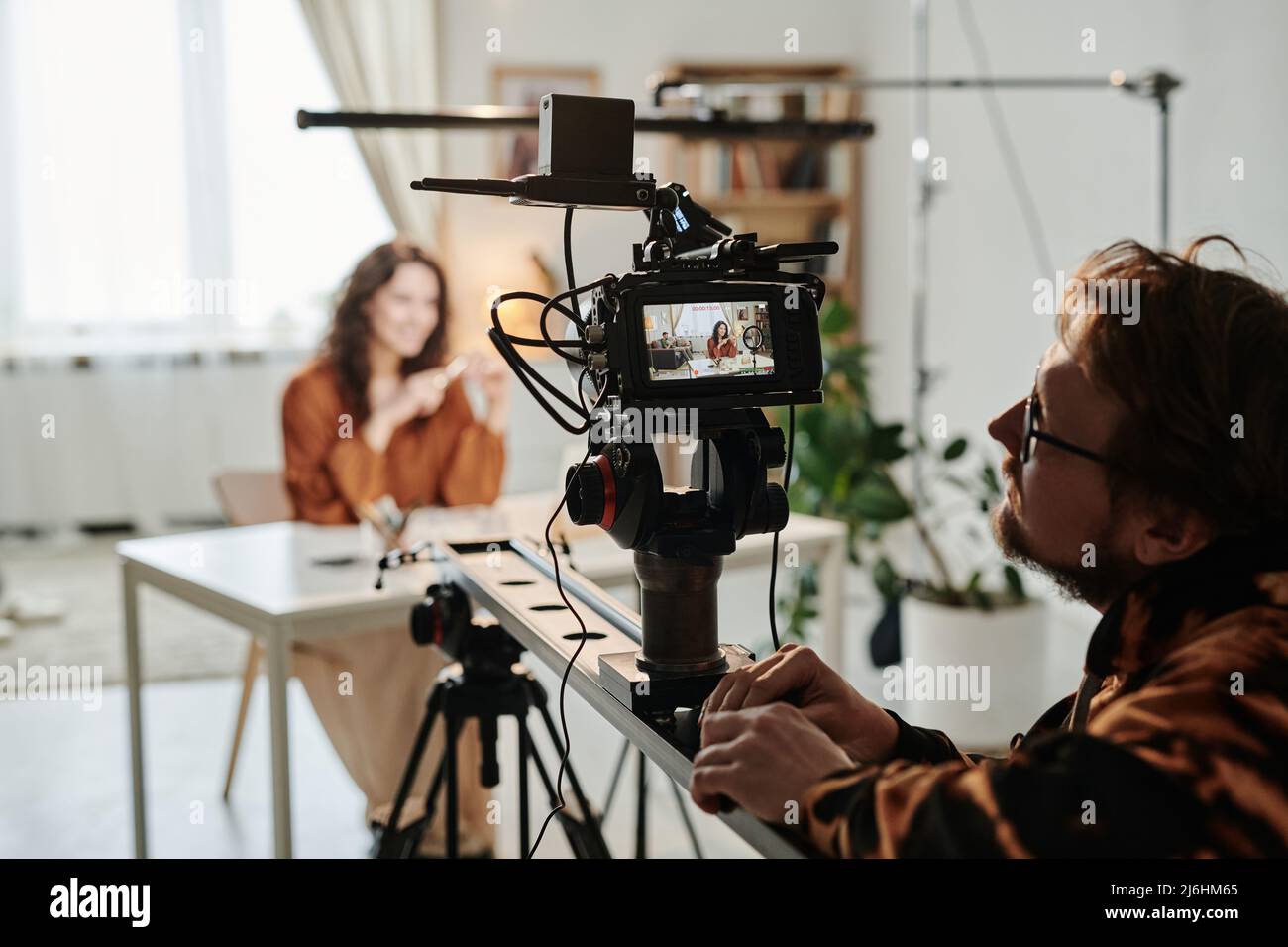 Young cameraman adjusting focus and other options of video camera ...