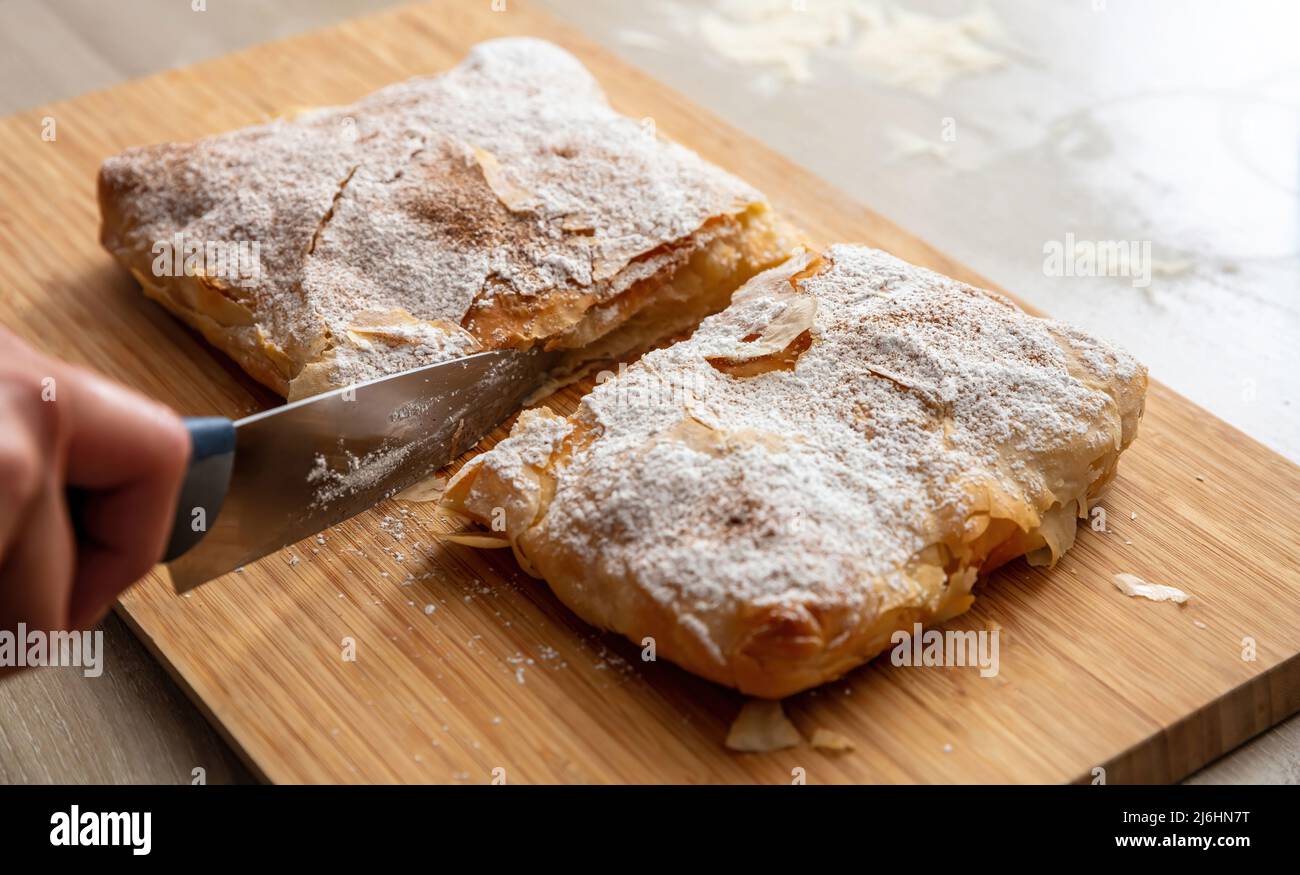 Greek pastry with cream sugar powder and ground cinnamon. Hand with a ...