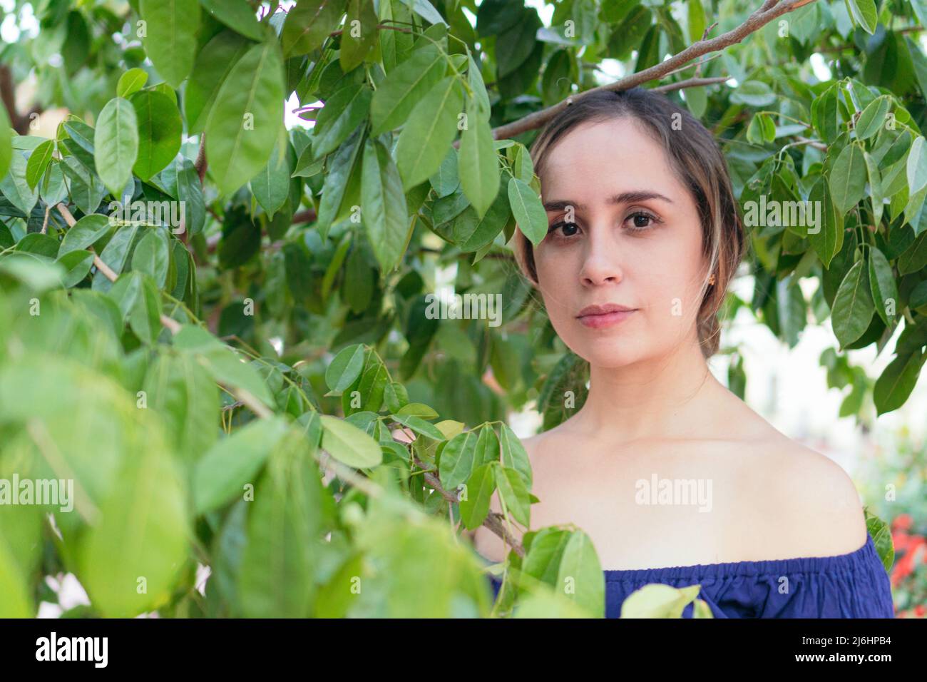 a young woman poses while surrounded by a variety of plants in a lush ...