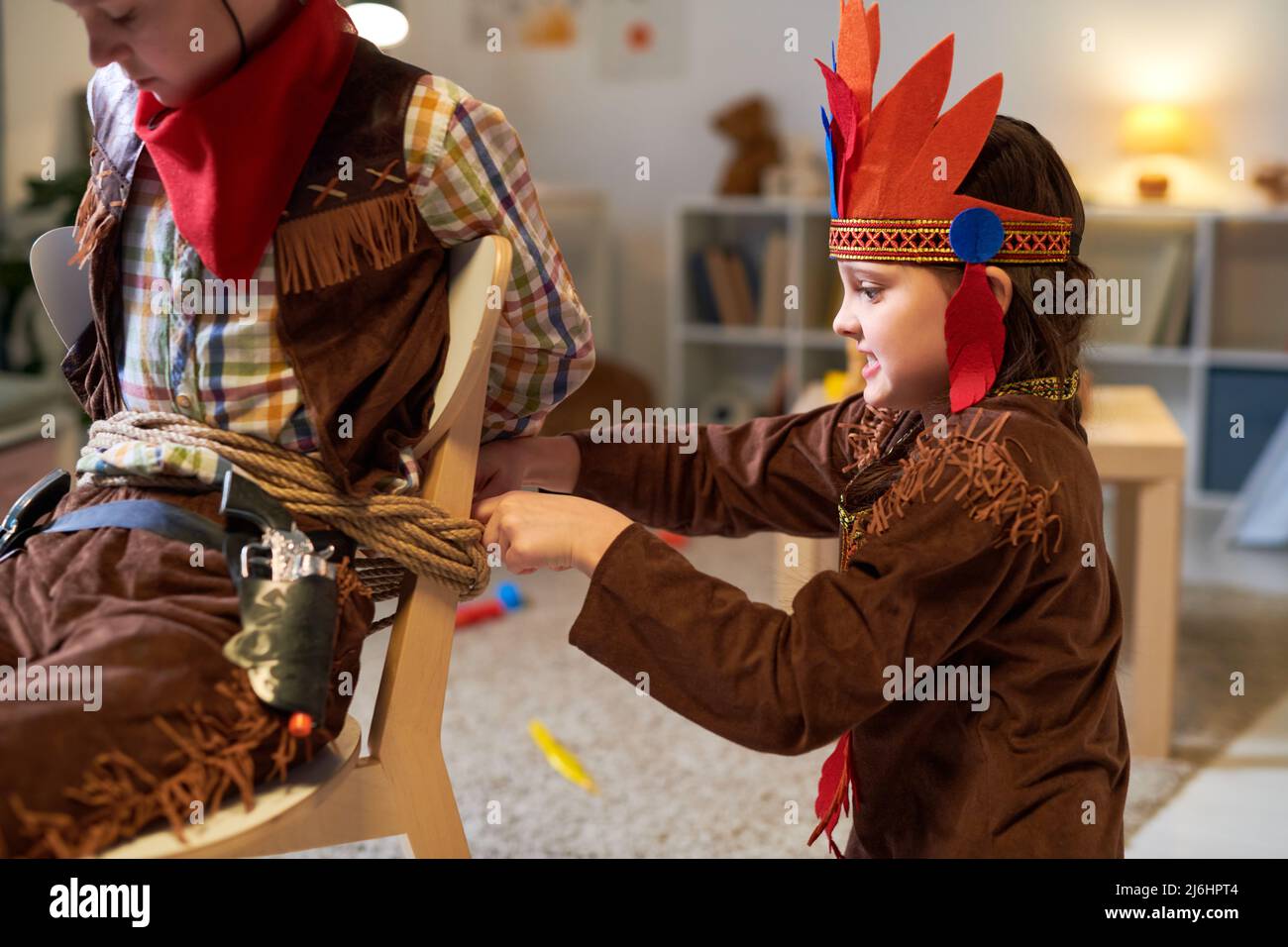 Little girl in native American costume binding cowboy to wooden chair ...