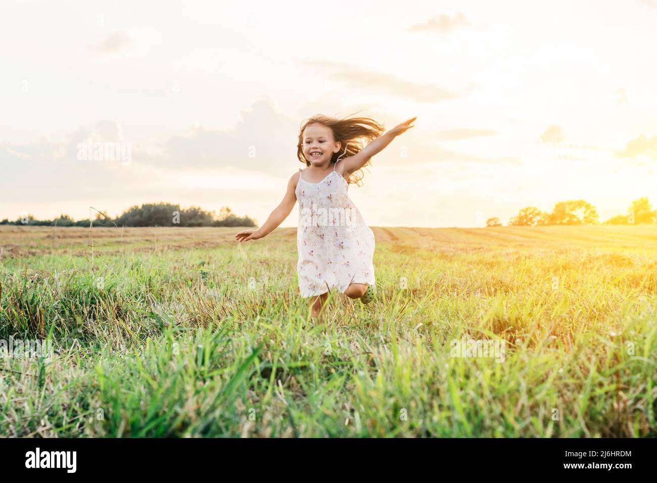 Portrait of smiling girl playing, jumping and running on grass hay ...