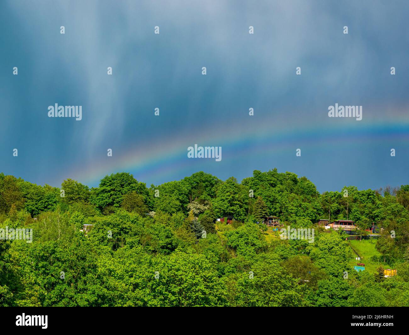 Rainbow over the hill with several garden houses a few moments after ...