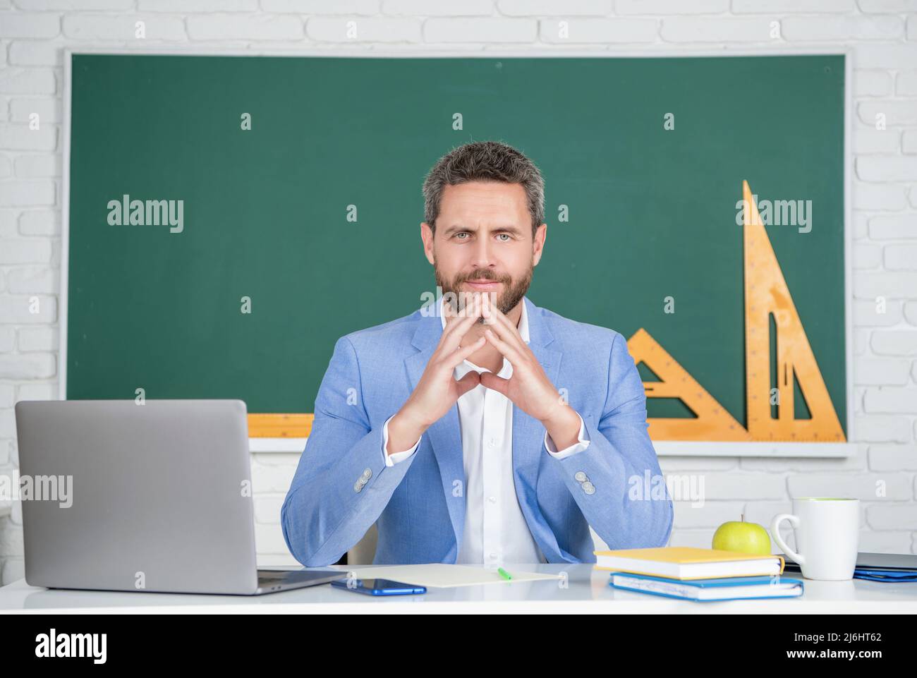 positive school teacher in classroom with laptop at blackboard Stock ...