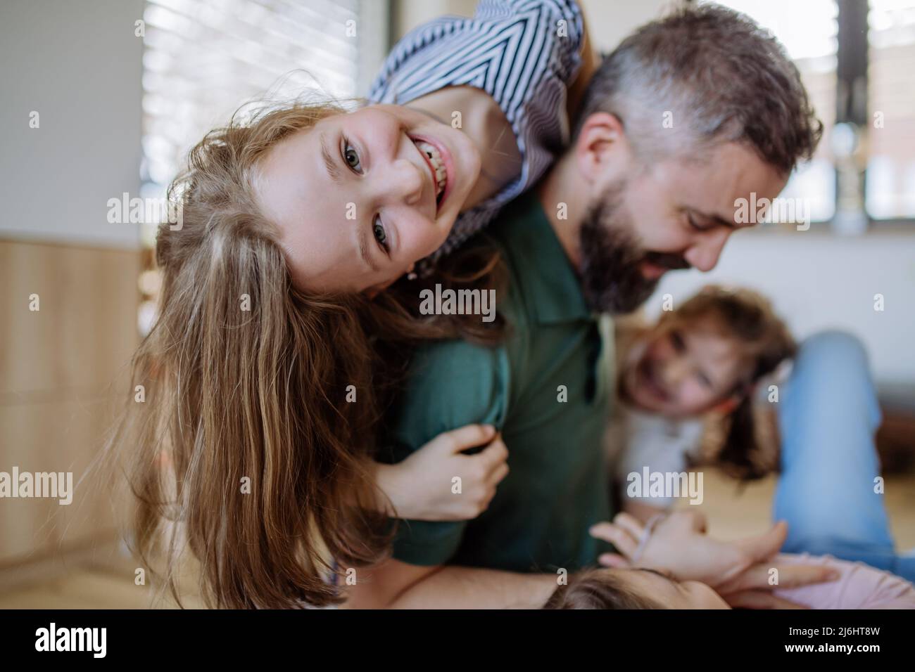 Cheerful father with three little daughters playing together at home ...