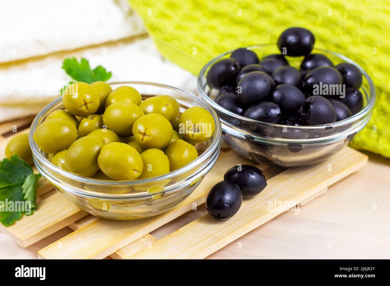 Many green and black marinated whole olives in the glass bowl on light ...