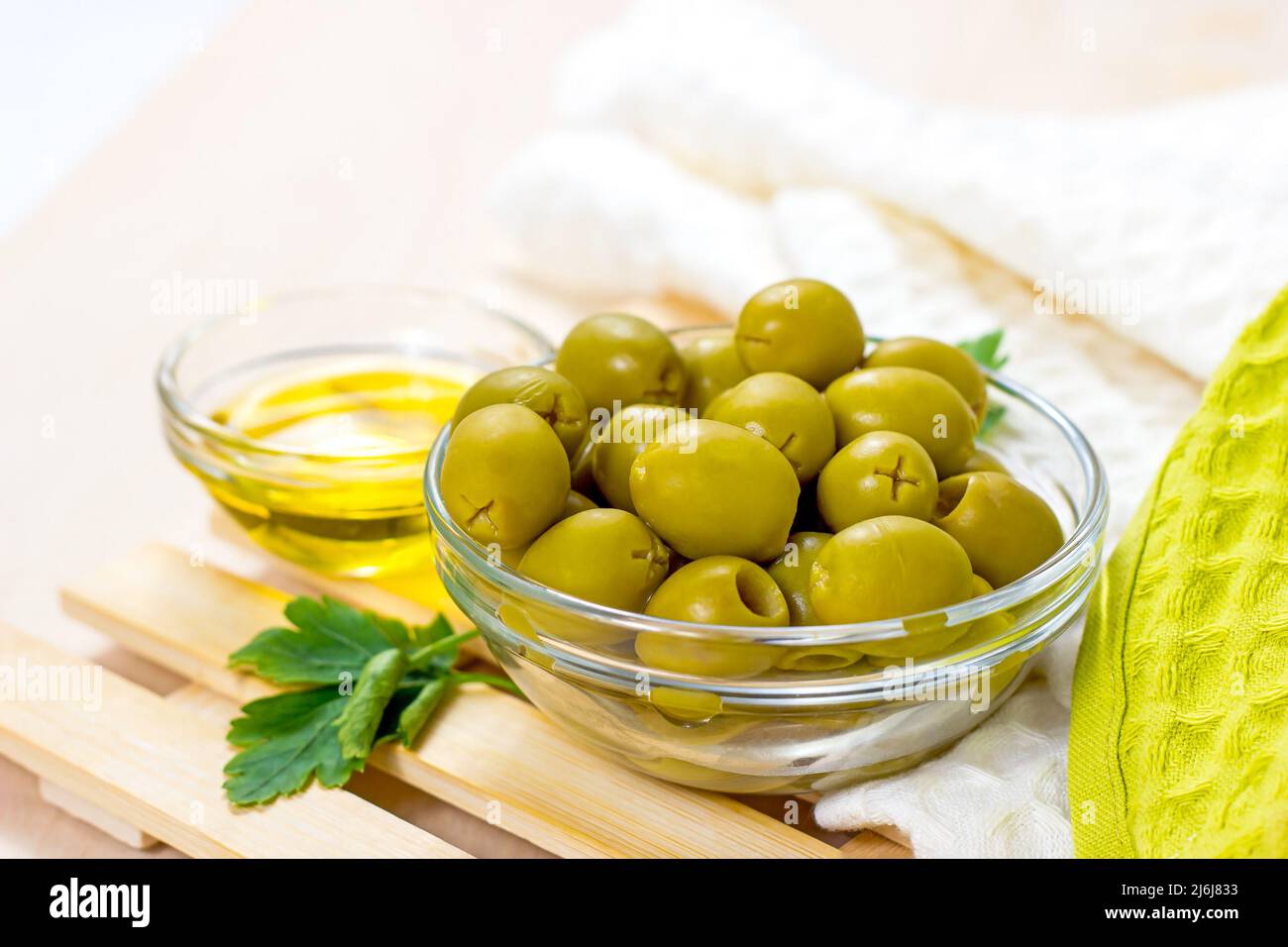 Many green whole olives and olive oil in the glass bowls on light ...