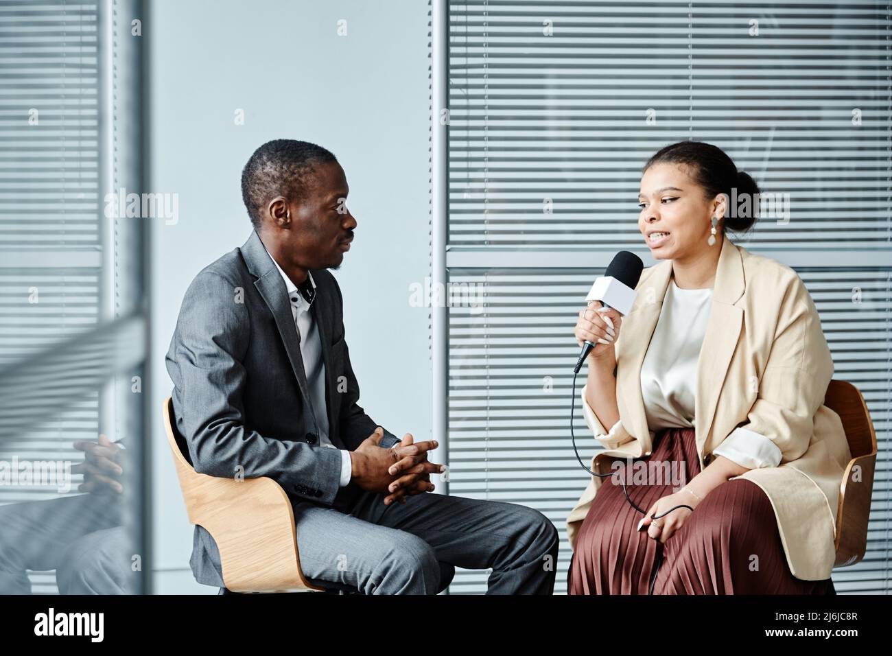 Portrait of young African American journalist speaking to microphone ...