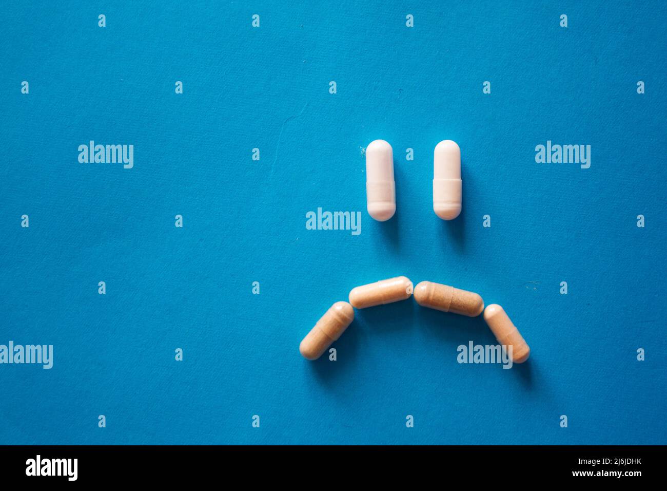 Sad face of pills on blue background Stock Photo - Alamy