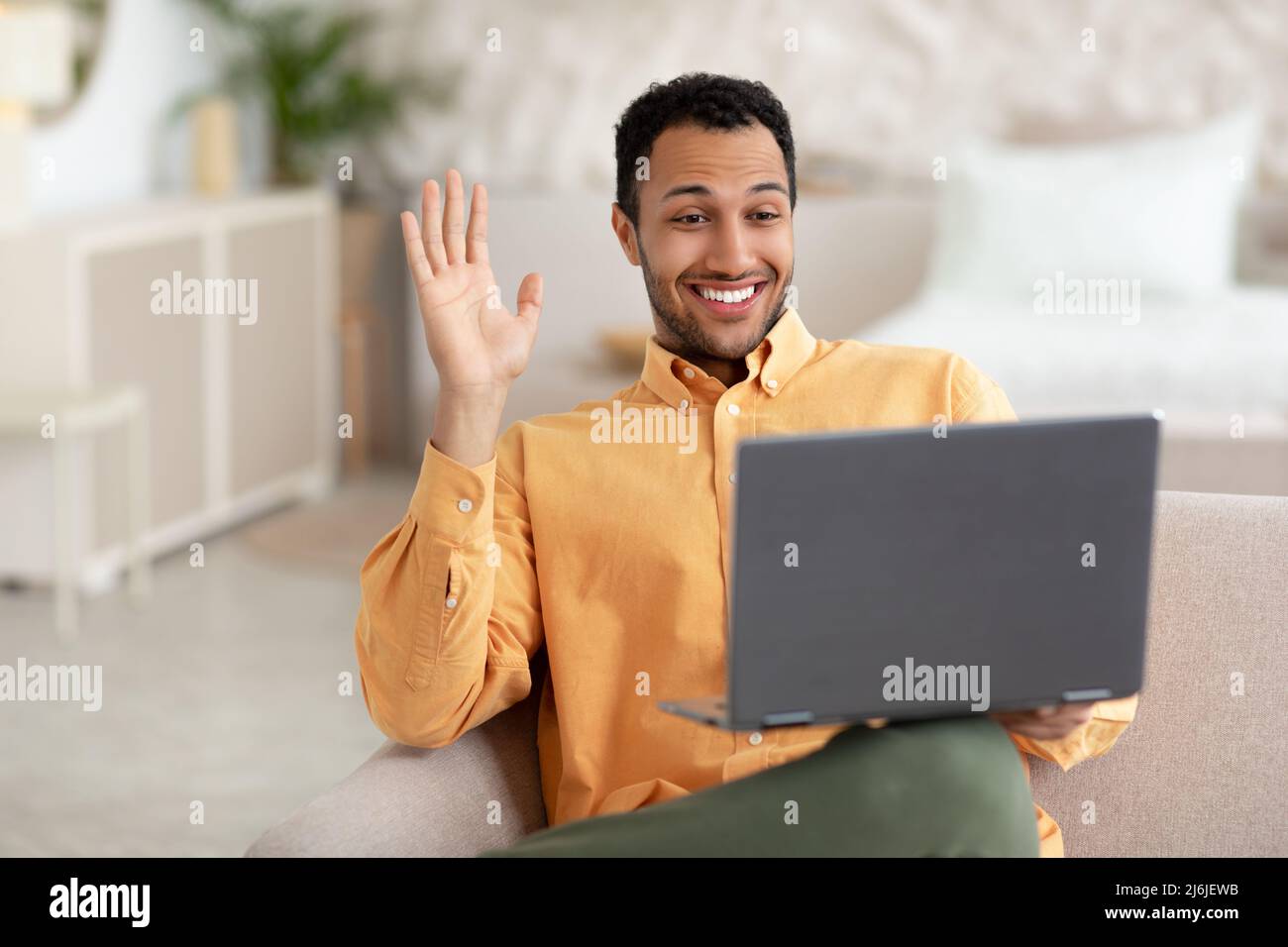 Smiling man working on laptop waving hand Stock Photo - Alamy
