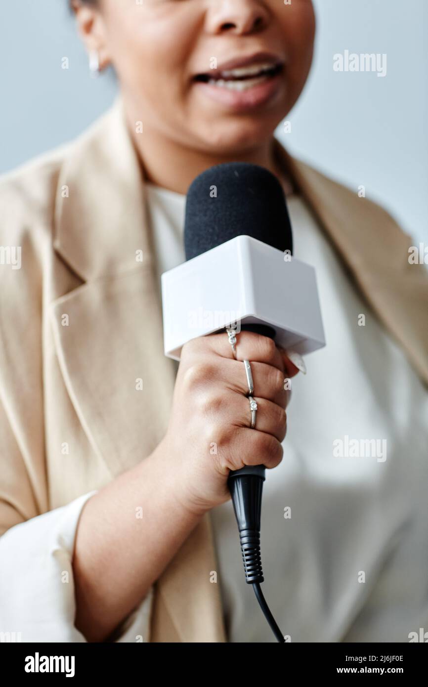 Vertical closeup of female journalist holding mic while reporting news ...