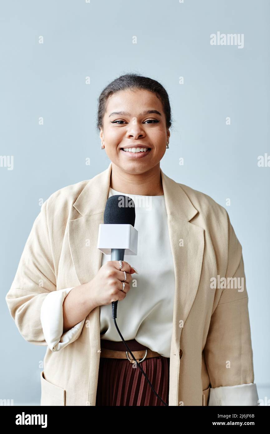 Minimal portrait of smiling female journalist holding mic while ...