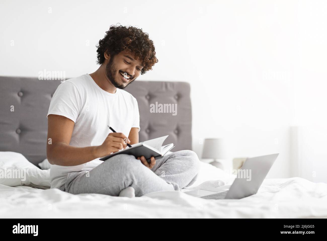 Dark-skinned guy in pajamas using laptop, taking notes Stock Photo - Alamy
