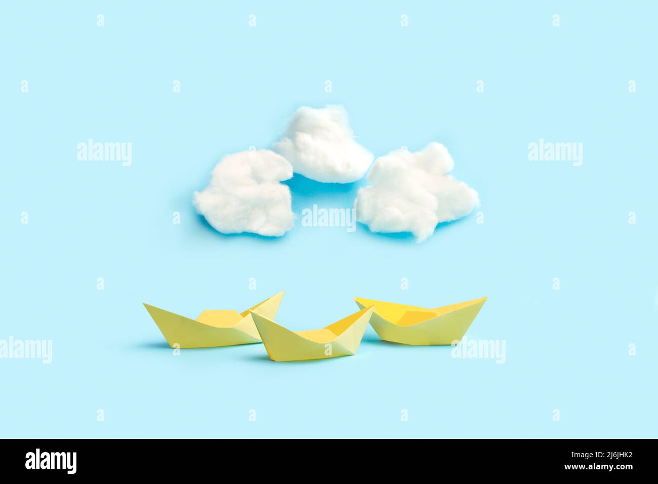 Yellow paper toy boats with white clouds shaped cotton on a light blue ...