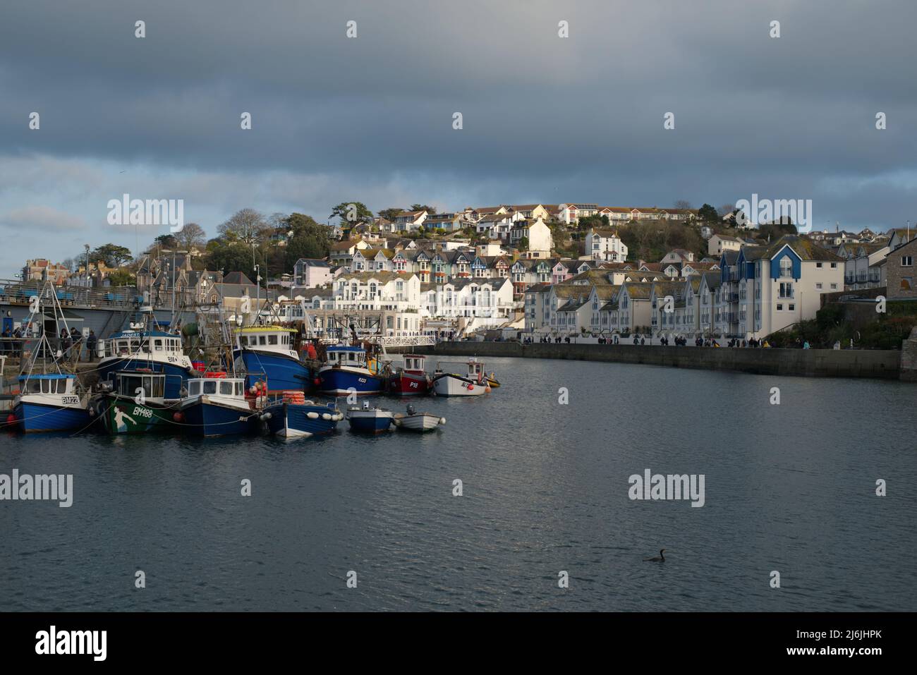 Boats, including sailboats, rest in Brixham Harbour. Terraced and ...