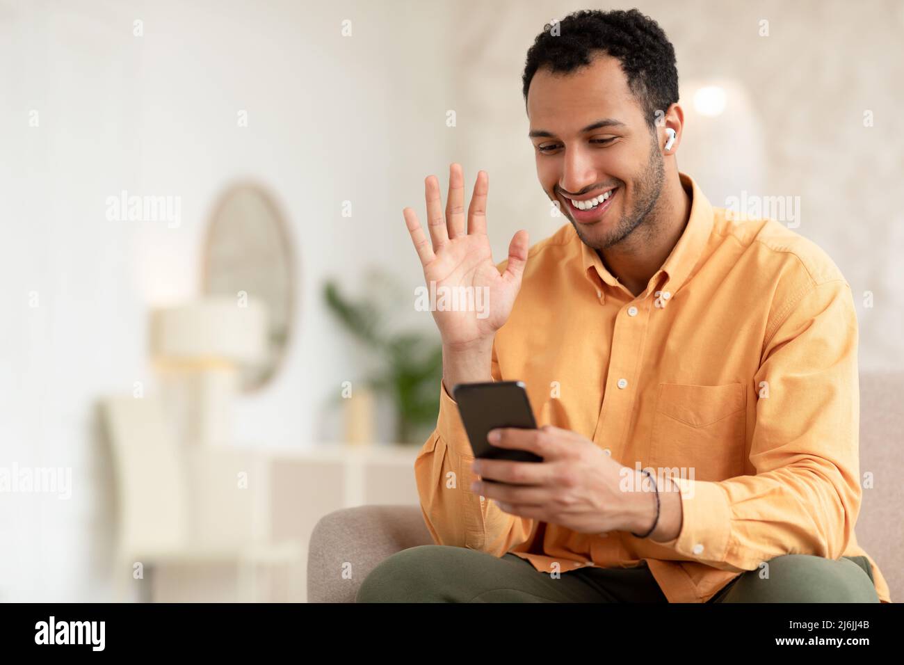 Smiling young man waving hand using mobile phone Stock Photo - Alamy