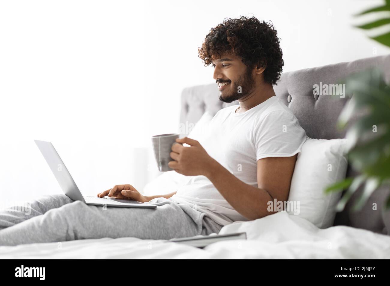 Relaxed indian man drinking coffee in bed, using laptop Stock Photo - Alamy