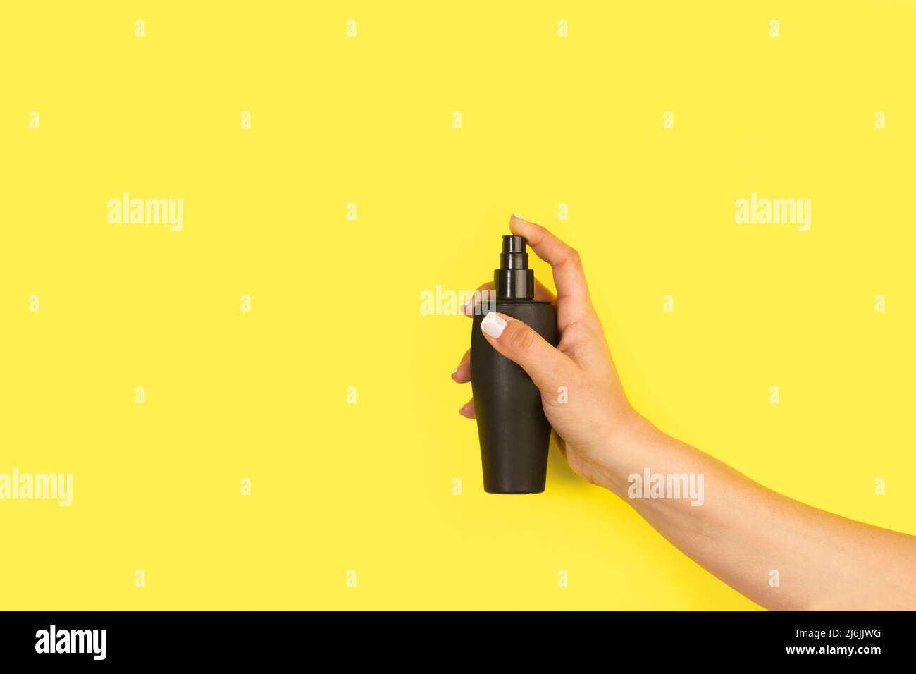 Woman hand holding a perfume sprayer on a yellow background with copy ...