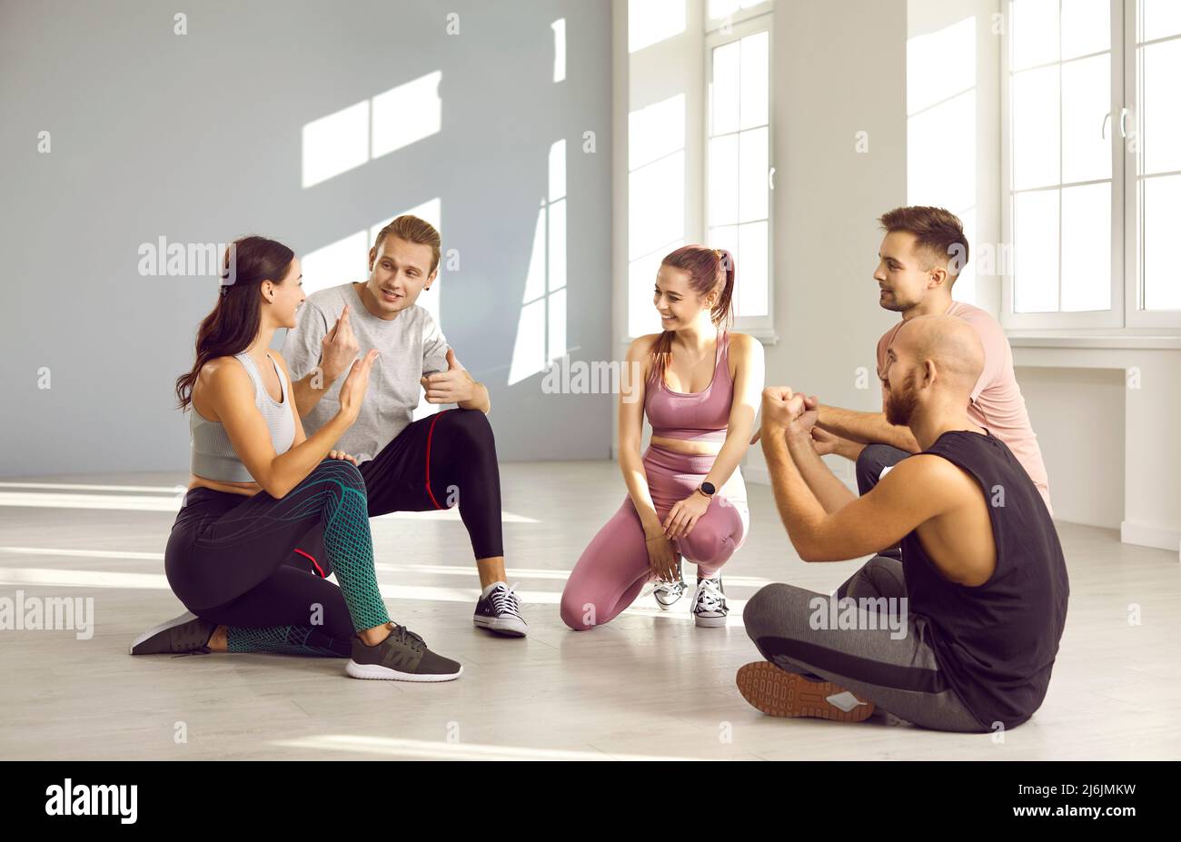 Group of happy young friends sitting on the gym floor after a fitness ...