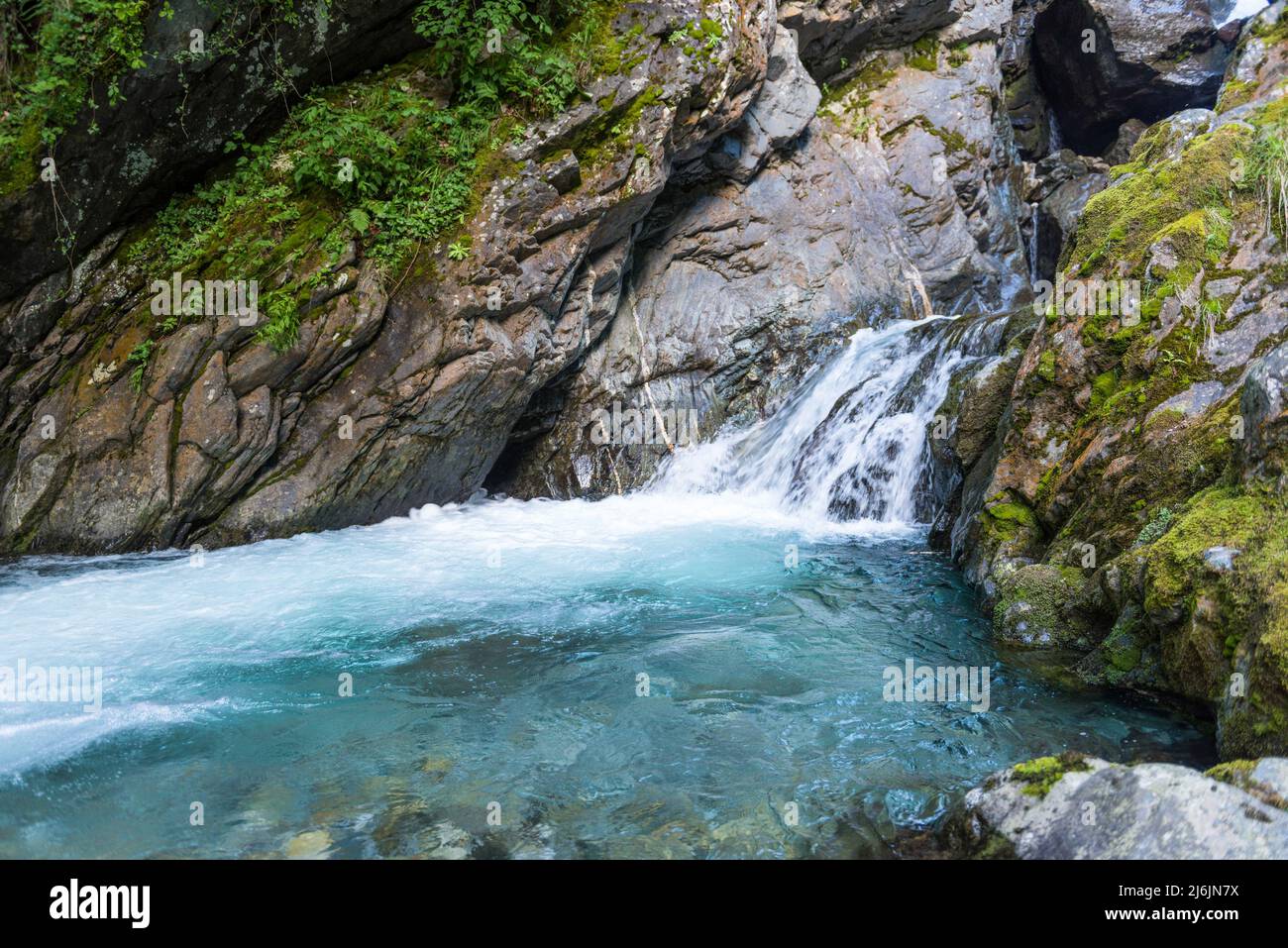 Fresh water from a mountain stream flows over rocks into a blue shining ...