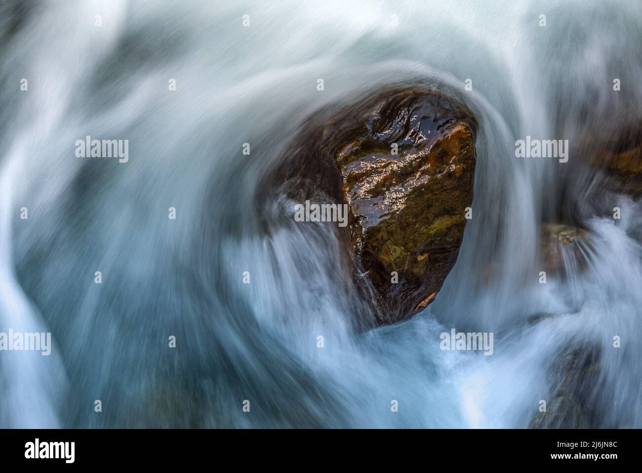 Water flows circularly around a rock photographed with motion blur ...