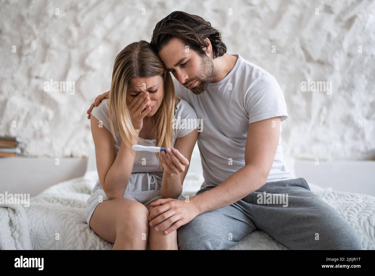 Upset young woman with negative pregnancy test crying on bed, loving ...