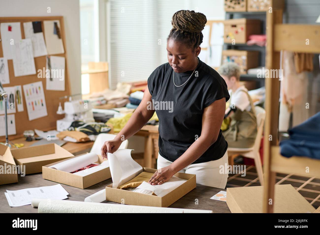 African American woman in casualwear standing by table and packing new ...