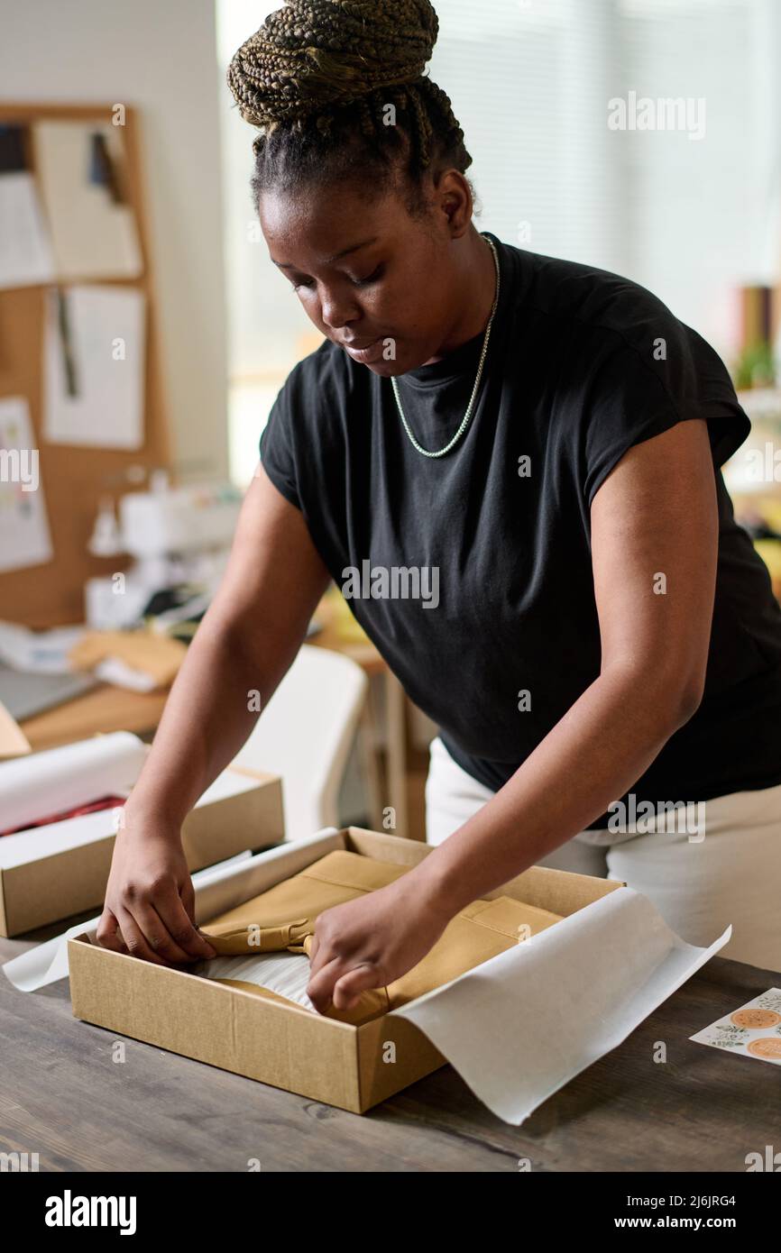 Young African American female worker of warehouse folding and packing ...