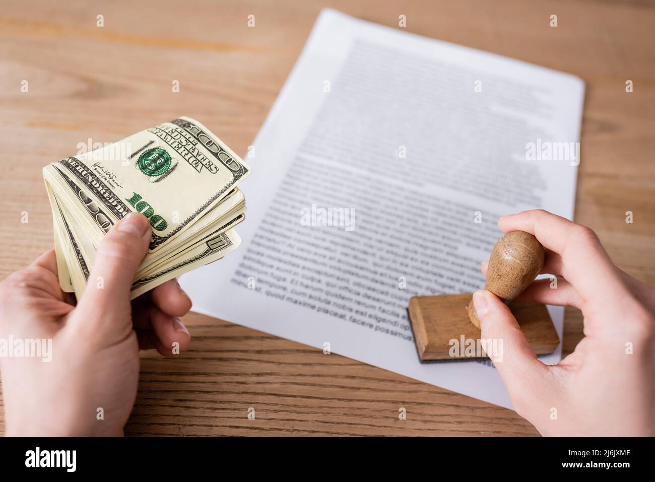 partial view of notary with dollars and stamper near blurred contract ...