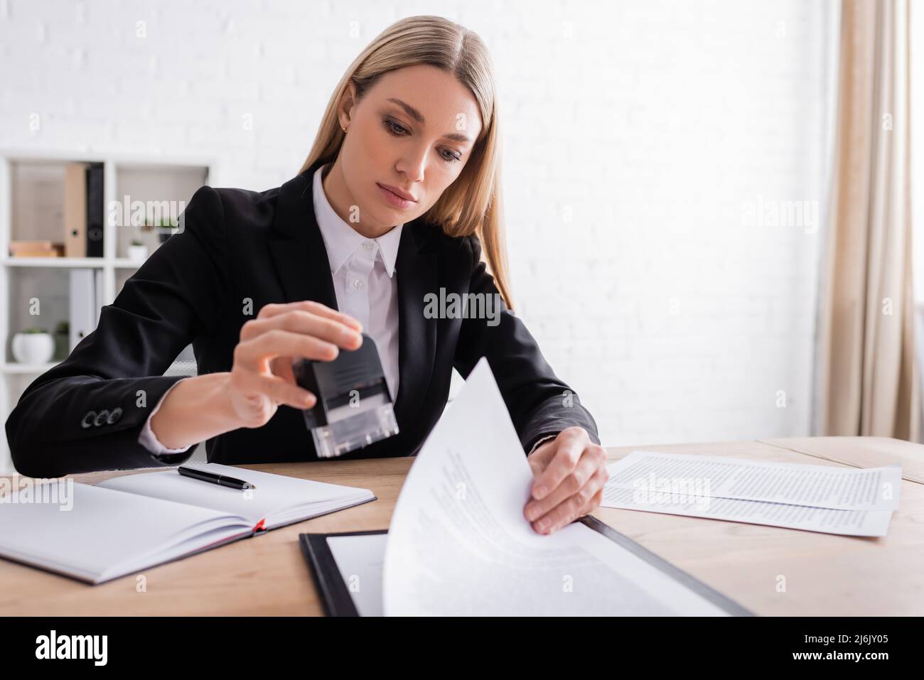 blonde notary holding stamper while working with documents in office ...