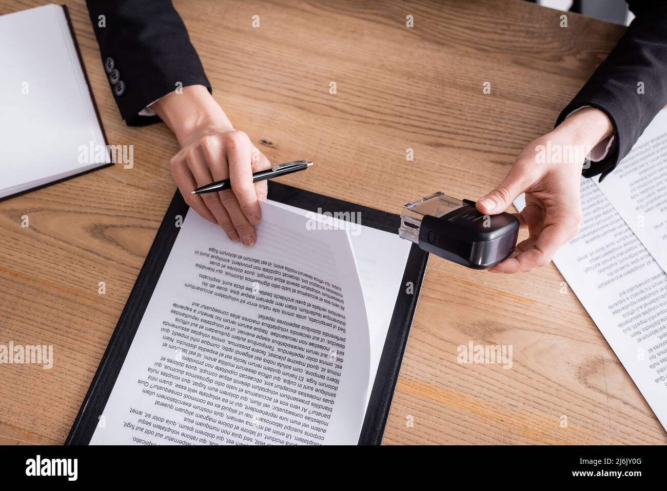 partial view of notary holding stamper and pen near documents on wooden ...