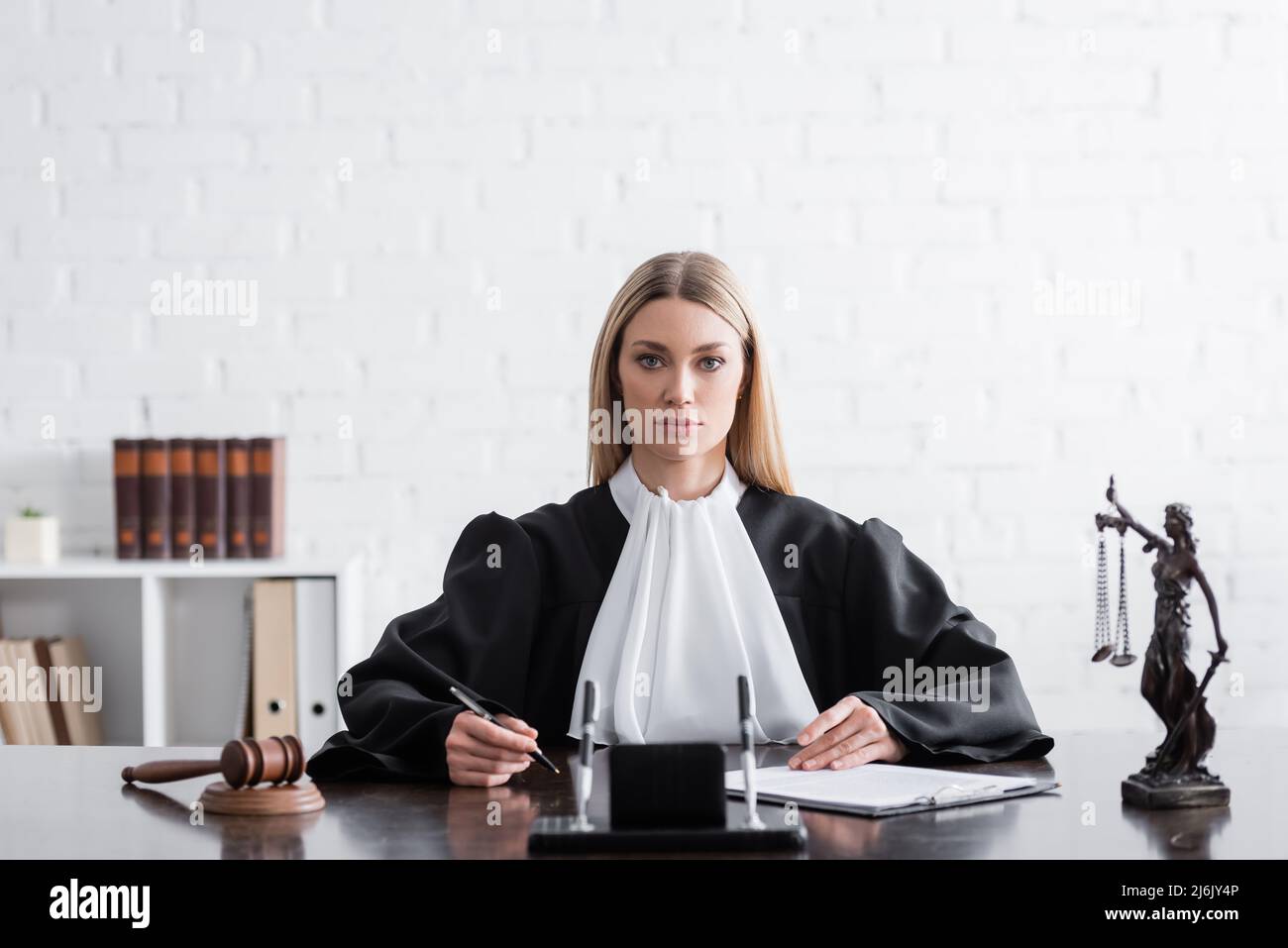 judge in mantle looking at camera while sitting near gavel and themis ...