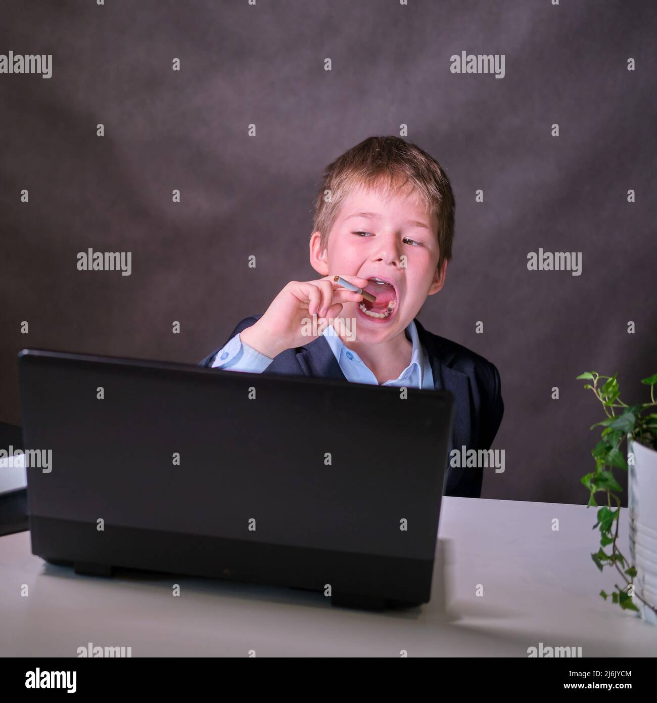 A boy in a school suit with a cigarette at the computer, copy space on ...