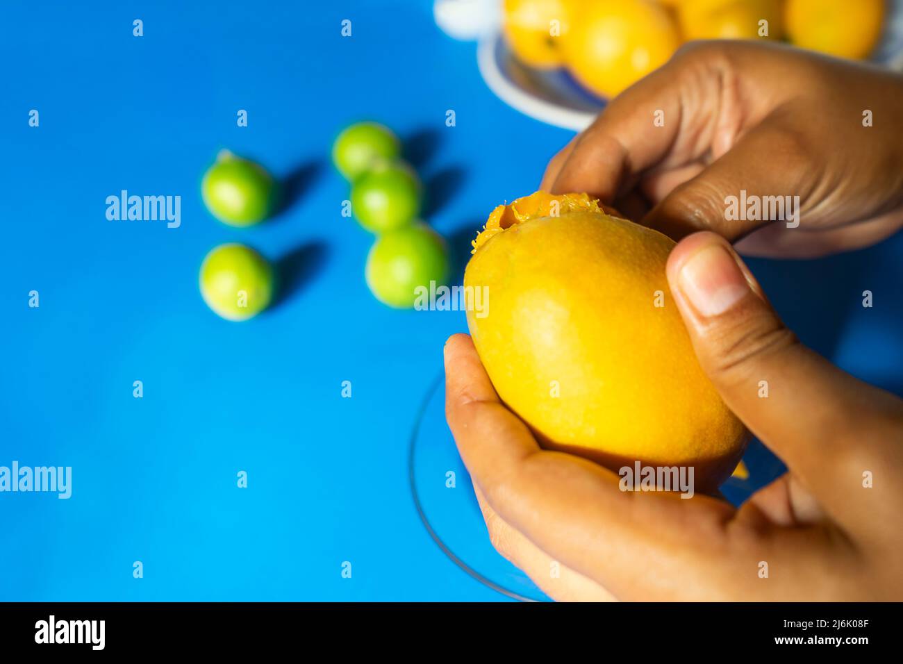 Closeup of the hand of a Latin woman peeling a mango with a blue ...