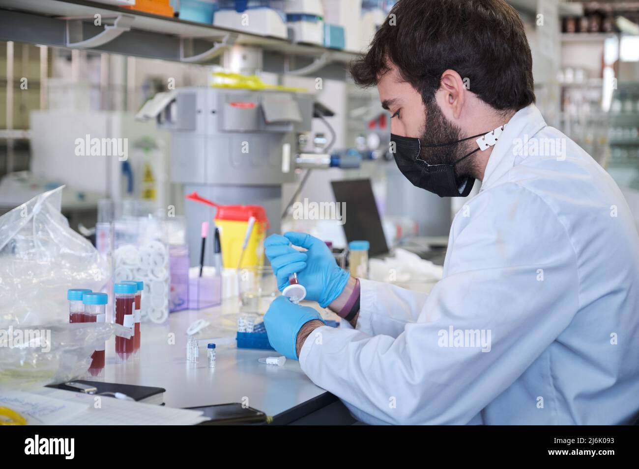 Scientist in white lab coat and face mask filter sample into HPLC vial ...