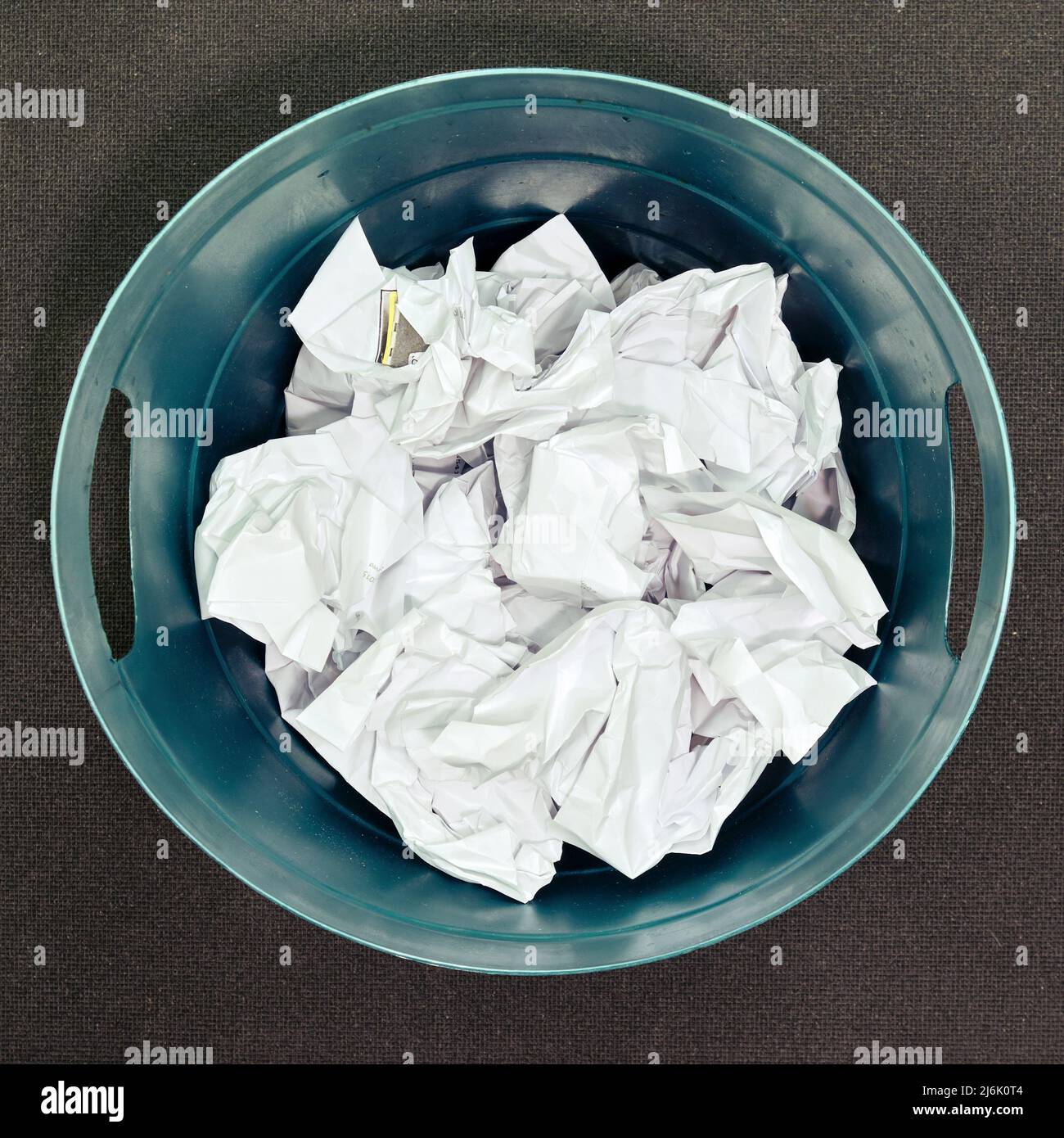 Plastic trash can being filled with crumpled sheets of white paper ...