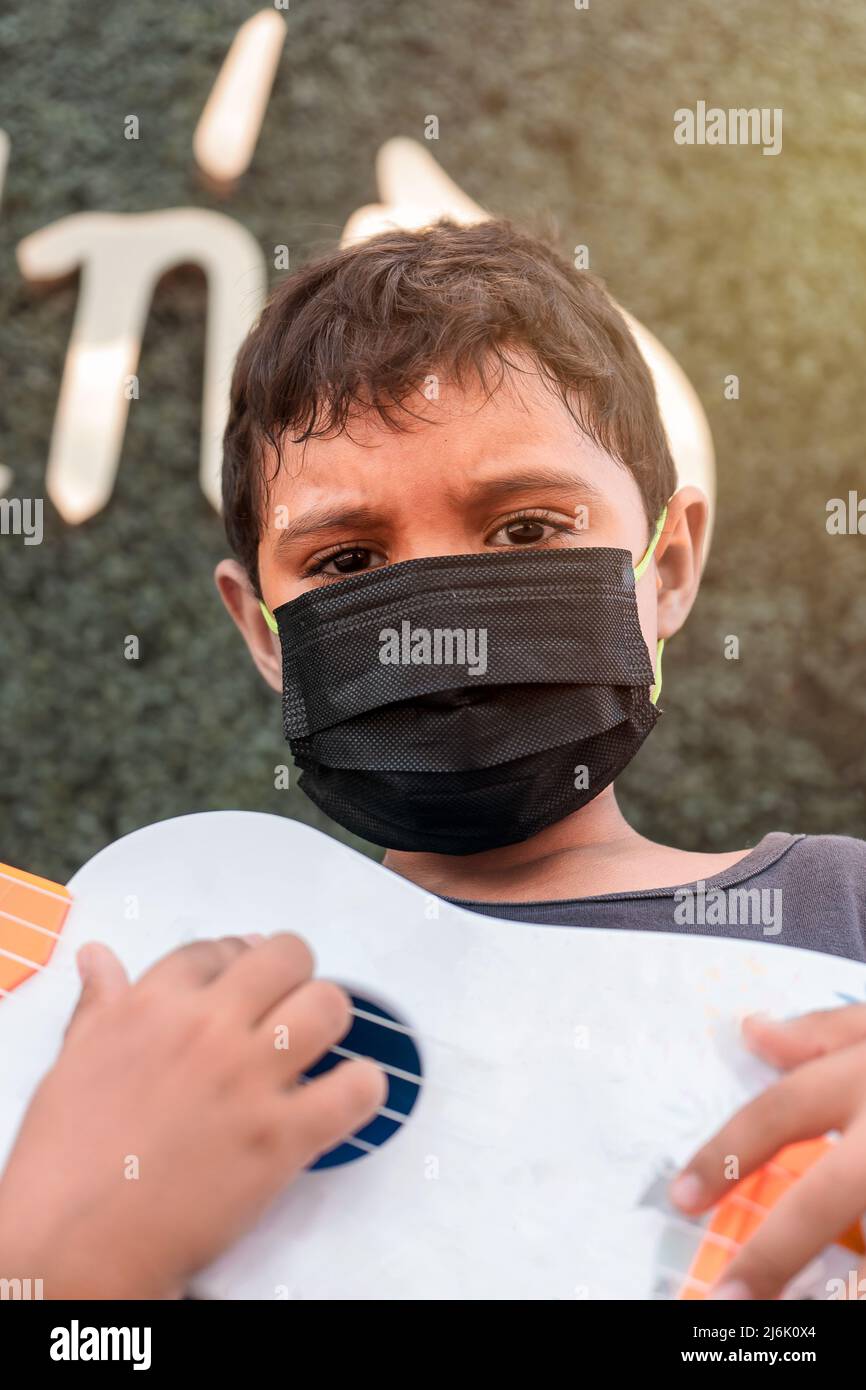 Vertical photo of a Latin boy with a medical mask outdoors looking at ...